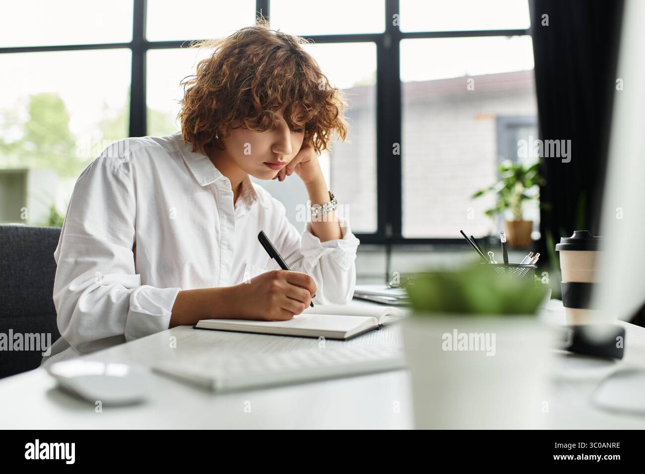 A young businesswoman with curly hair writes notes in her modern office ...