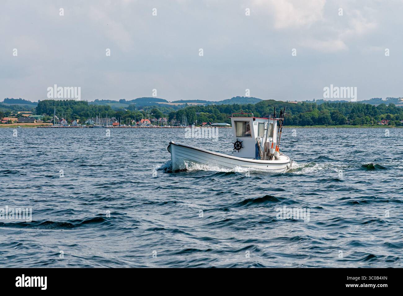 A white fishing boat navigates smooth waters, surrounded by lush green ...