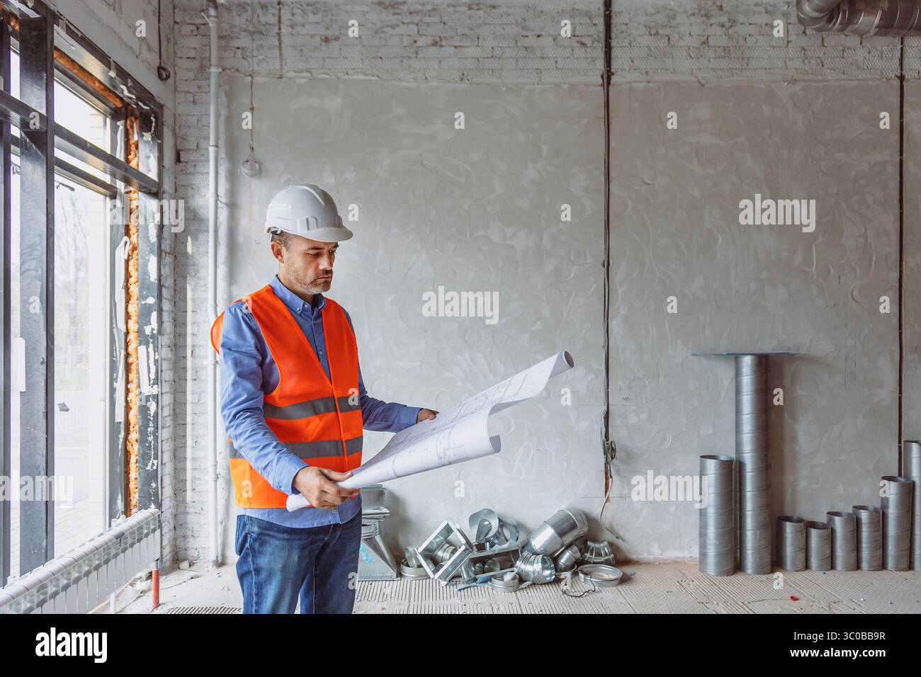 A construction worker wearing a safety vest and helmet focuses on ...