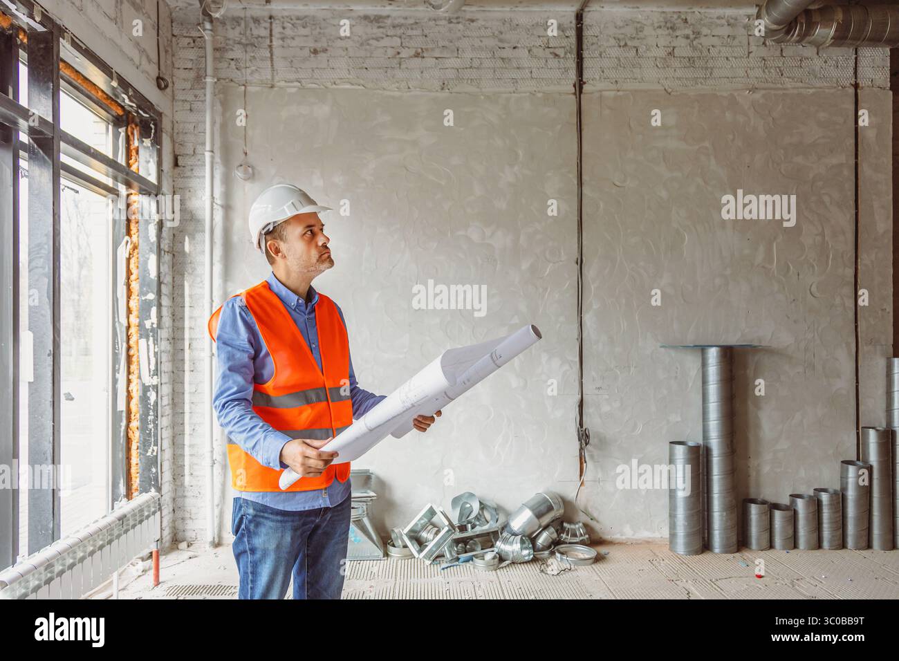 A construction worker wearing a safety vest and helmet focuses on ...