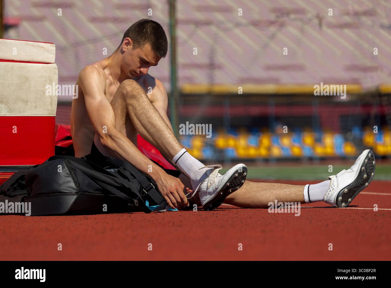 Athlete lacing up shoes on running track under sunny sky Stock Photo ...