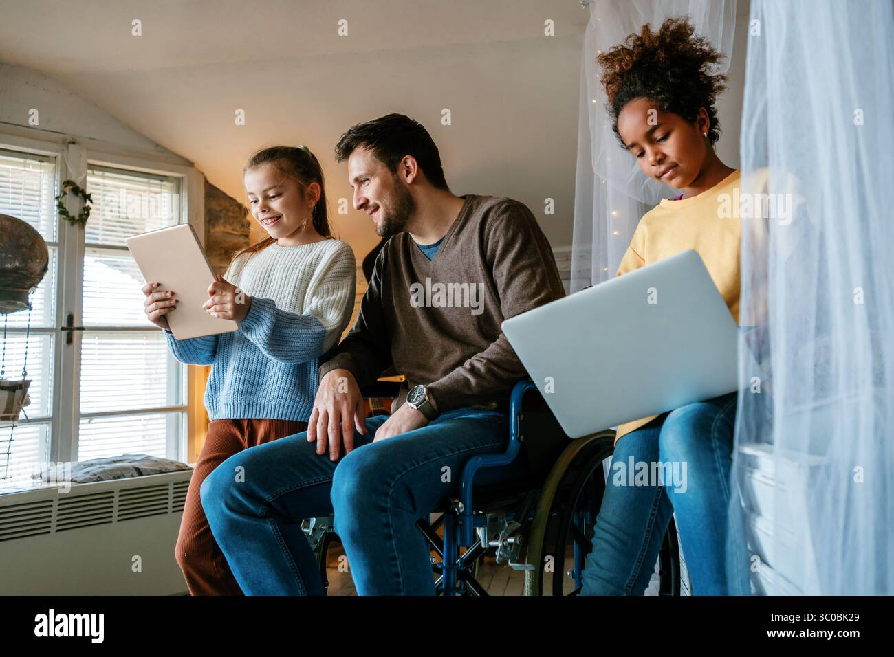 Happy father in wheelchair with interracial daughters using laptop together, education, fun ...