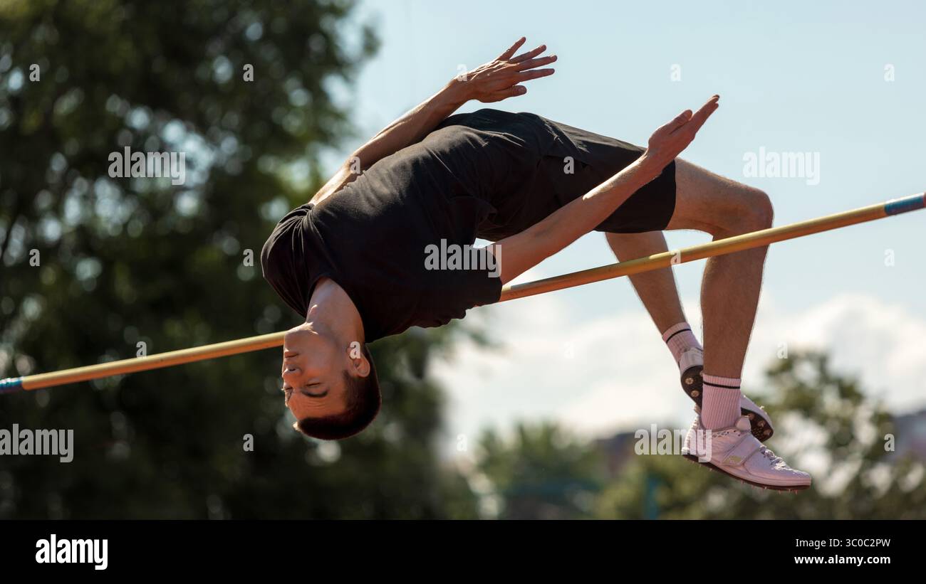Athlete in mid-air clearing high jump bar under clear sky Stock Photo ...