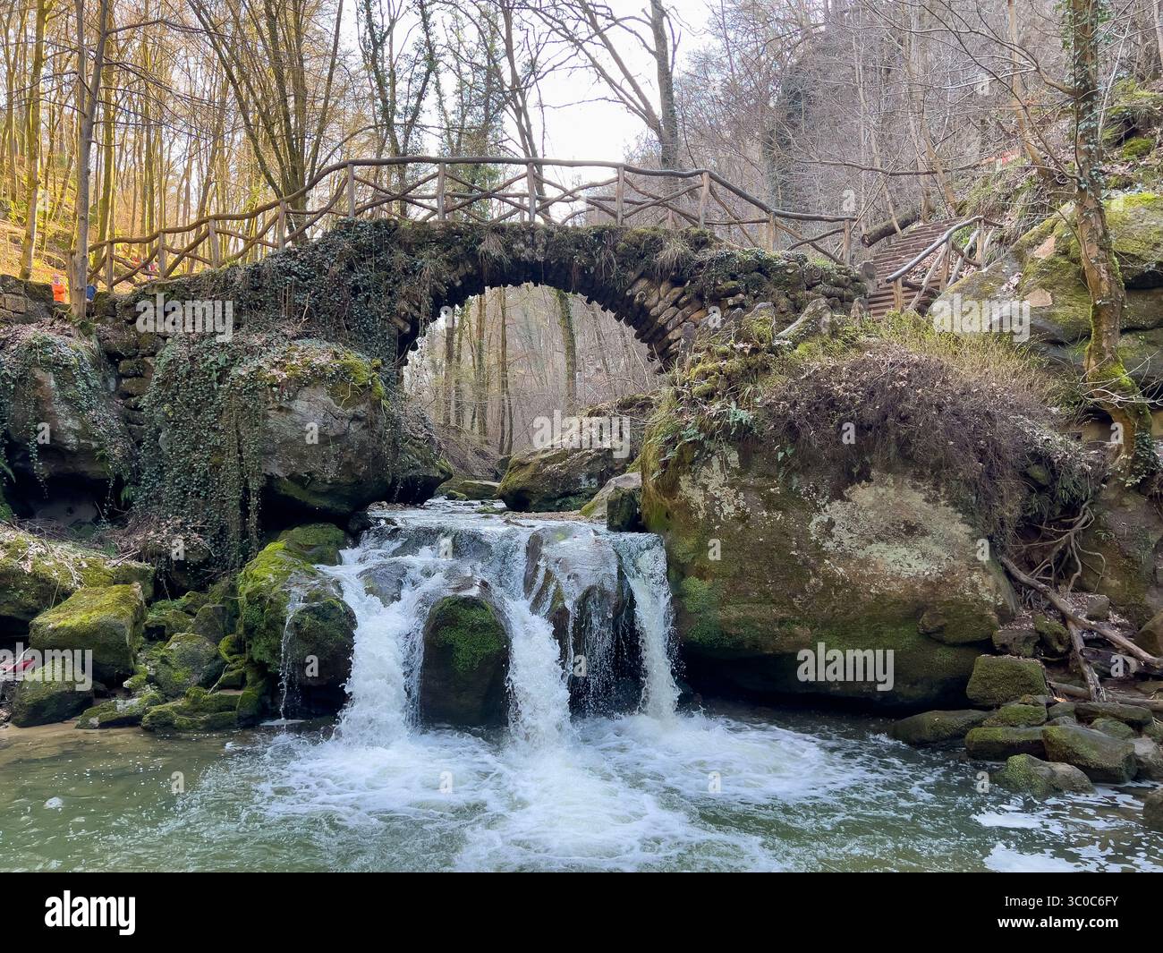View of a river crossed by an old arched bridge, Mullerthal in spring ...