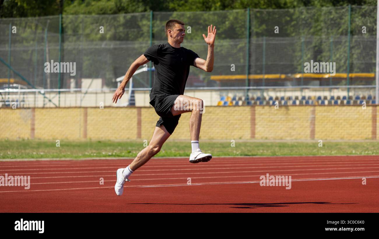 Youthful male runner dashing along an outdoor track beneath a sunny sky ...