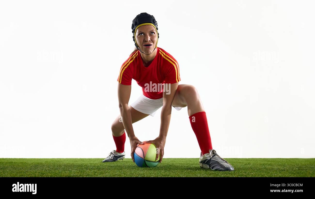 Rugby athlete in red attire stands ready with vibrant ball on green ...