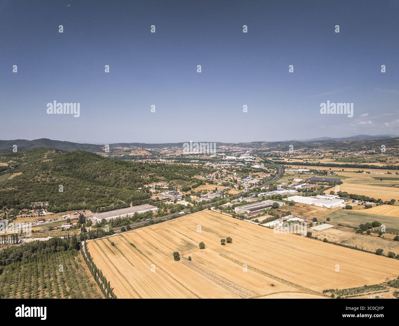 Aerial view of sun-kissed fields meet lush hillsides, buildings nestled ...