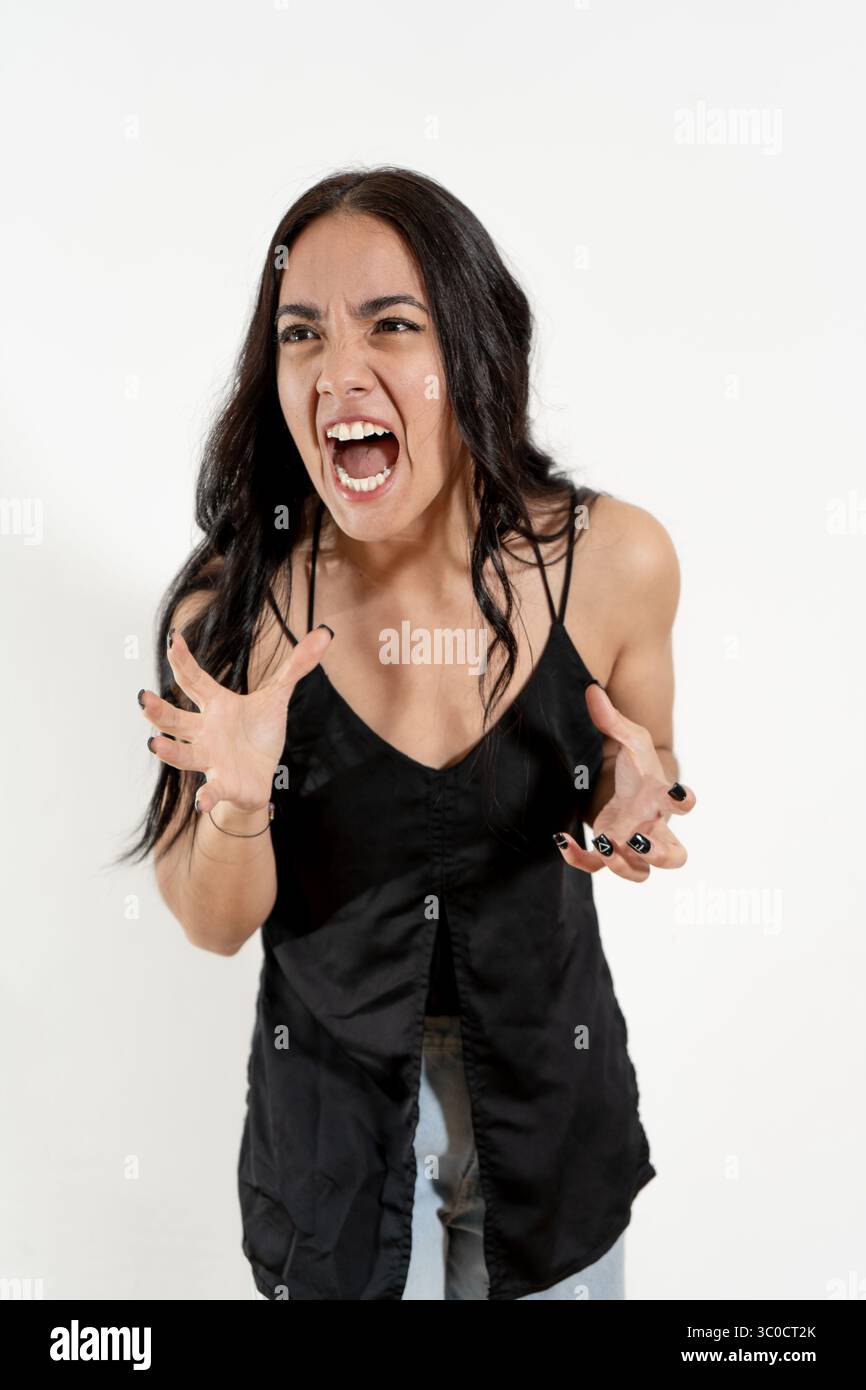 Studio portrait of a furious young woman shouting with raised hands and ...