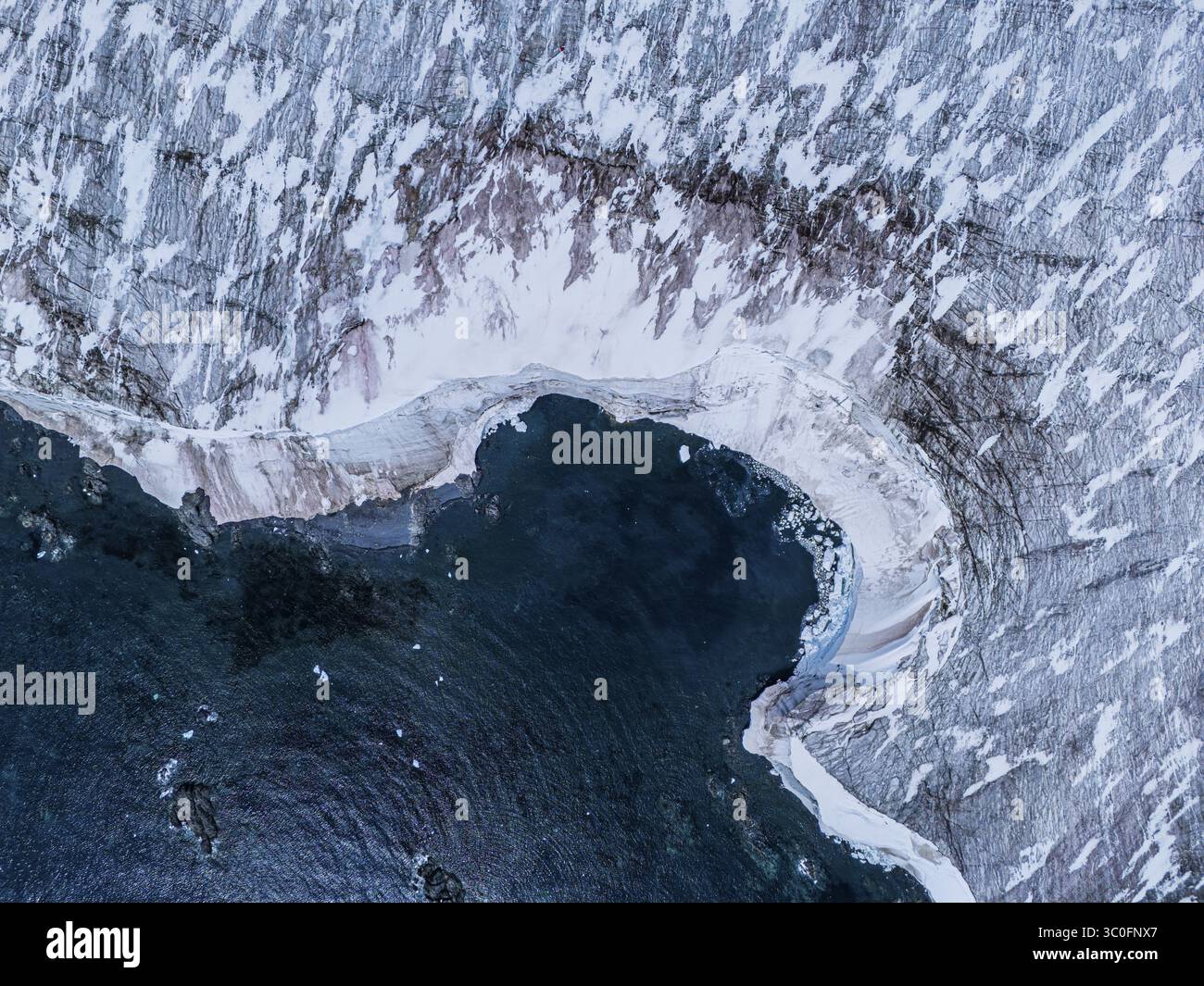 Aerial view of the stark contrast of dark blue water against the snow ...