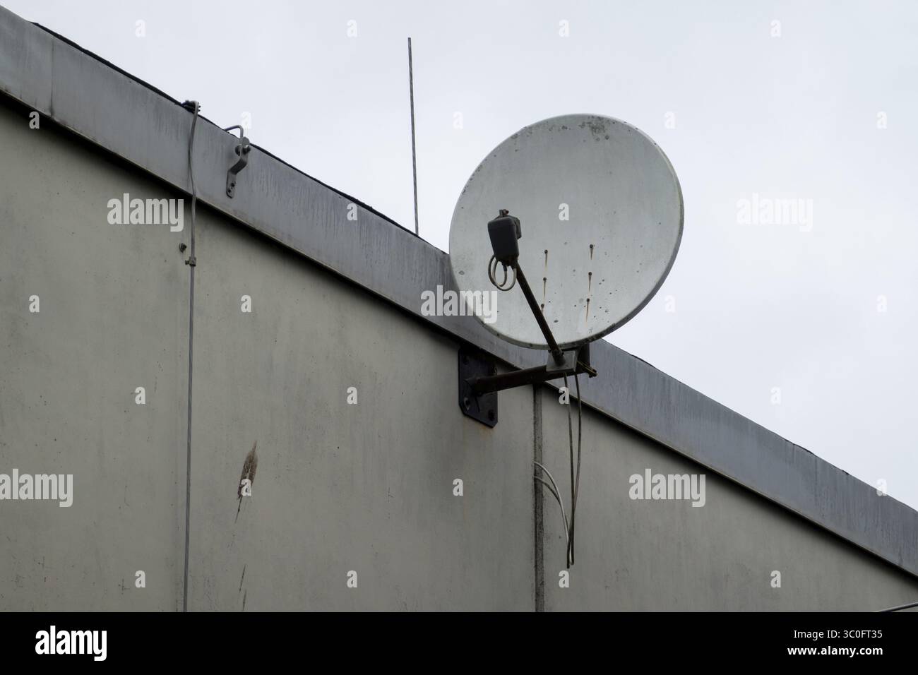 White satellite dish capturing signal on a gray building under a cloudy ...