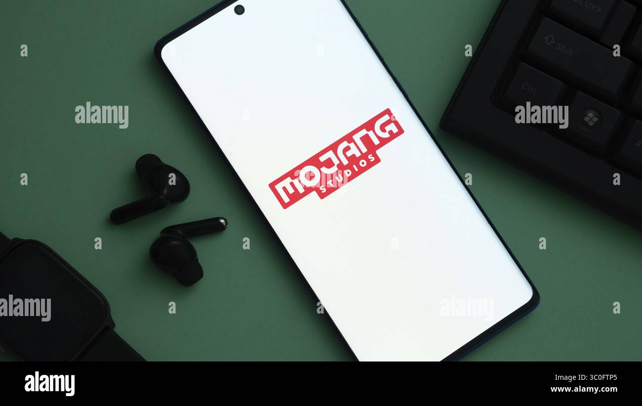 Mojang Studios logo on a smartphone screen with earbuds and a watch on ...