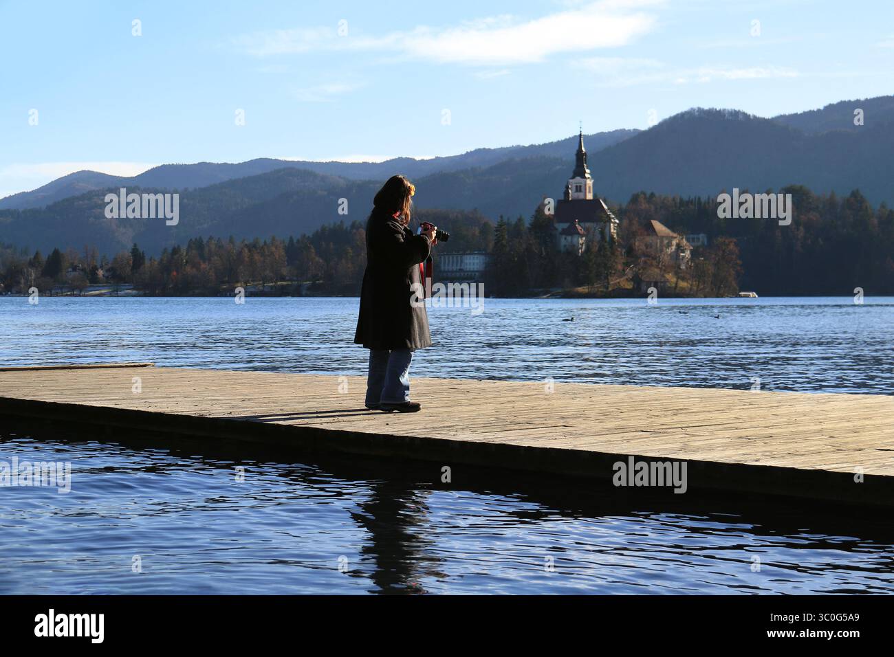 A woman photographer with her red camera standing on the pier of Lake ...
