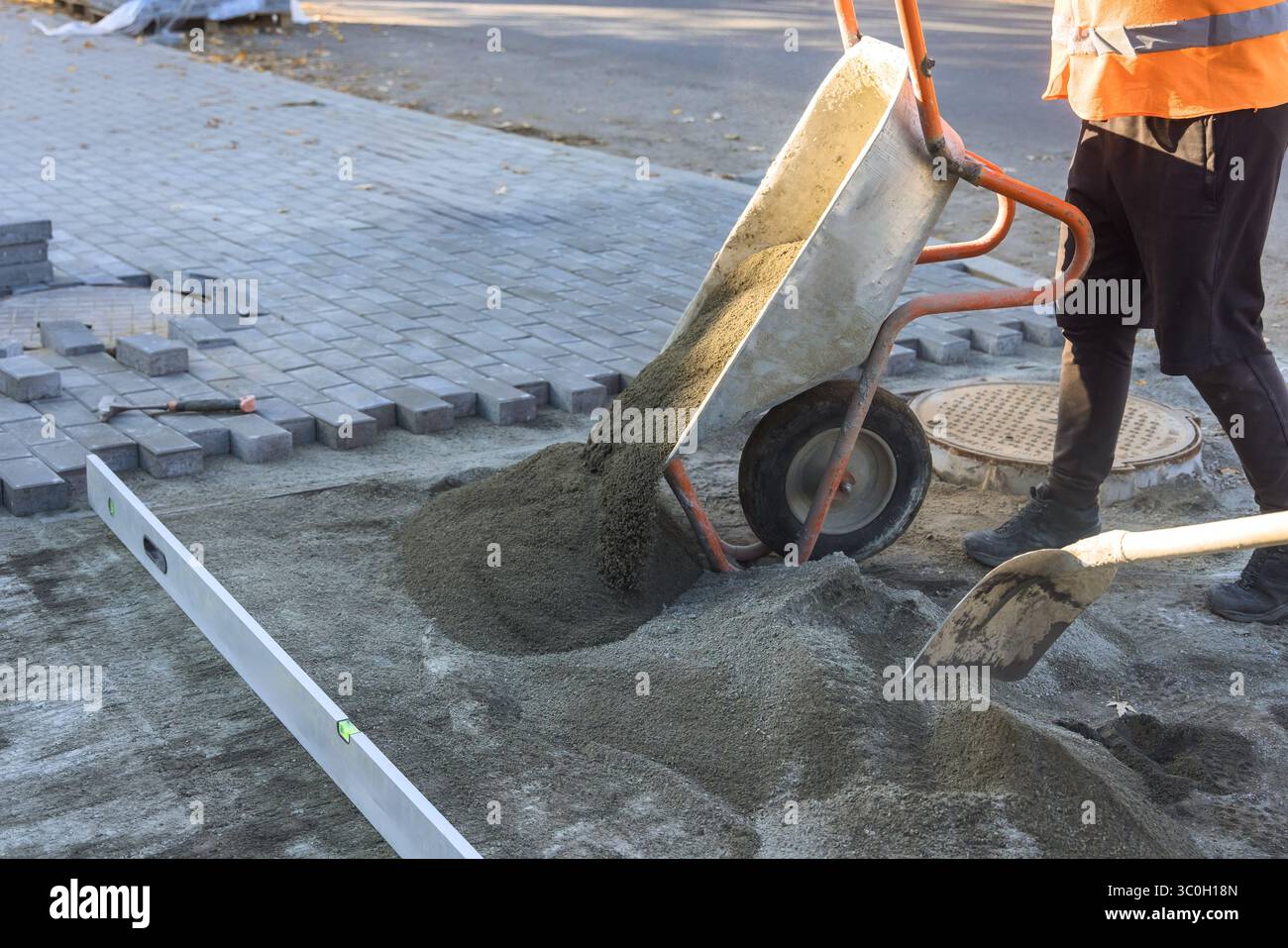 Construction worker pours sand from wheelbarrow onto ground to prepare ...