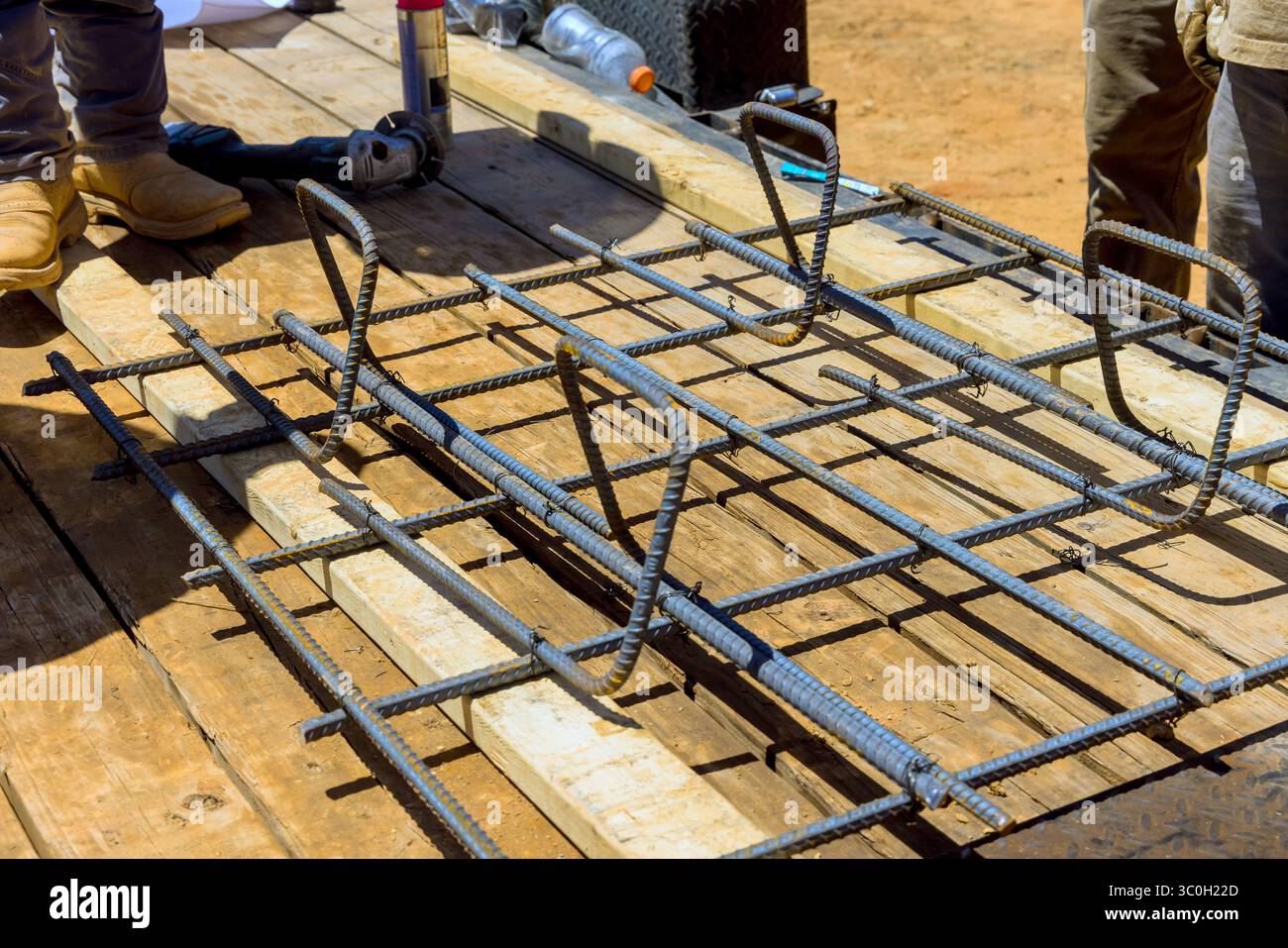 Workers prepare steel reinforcement bars on wooden platform under work ...