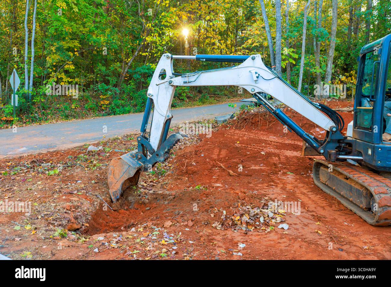 An excavator is actively digging dirt trench along gravel road with ...