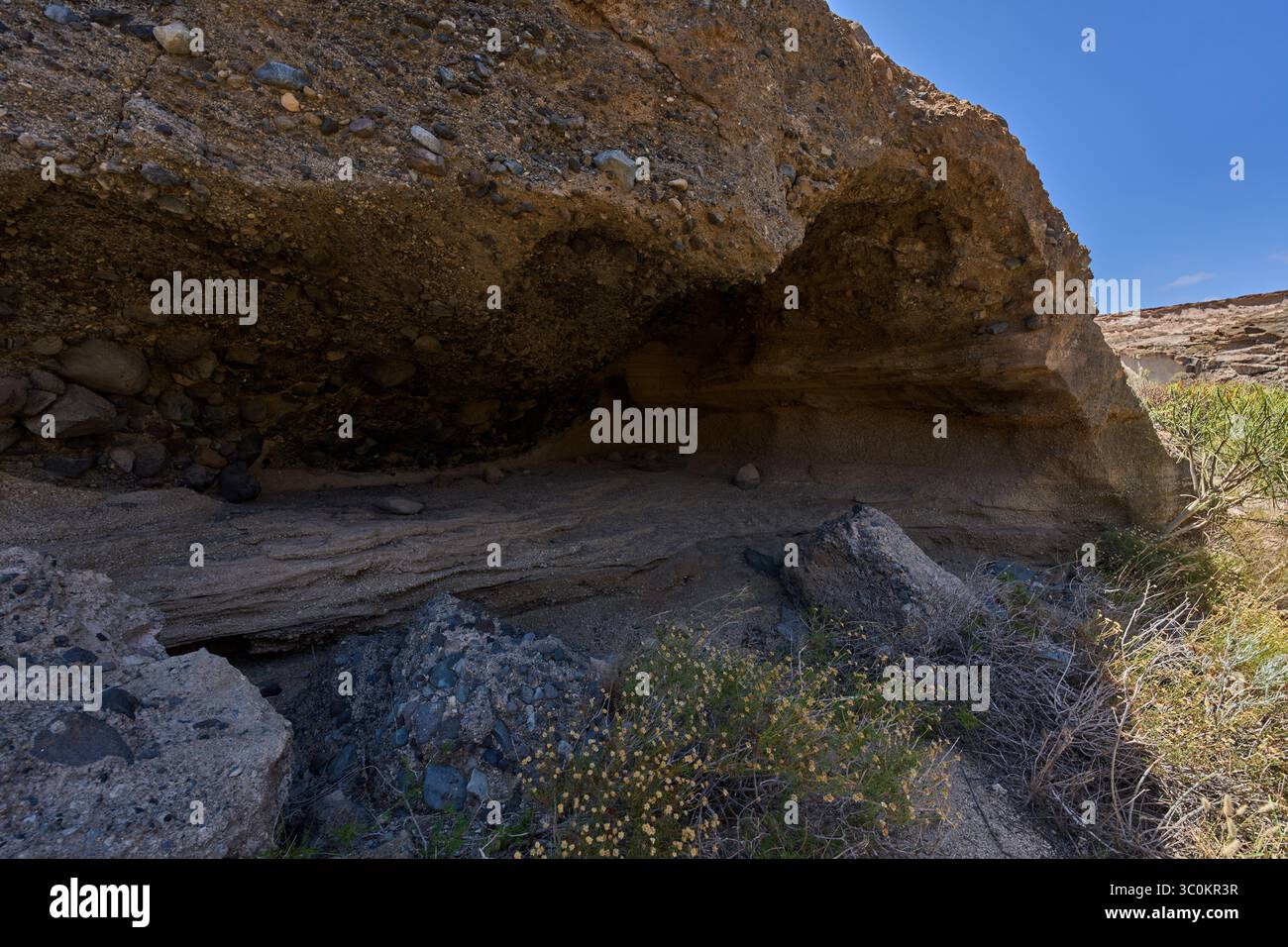 Shallow volcanic cave carved into eroded sediment layers with visible ...