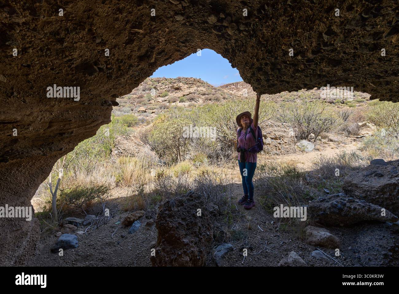 Female hiker reaching up to touch the ceiling of a volcanic cave while ...