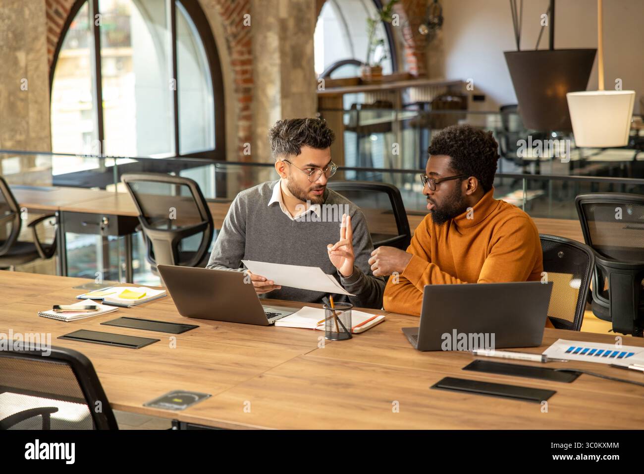 Two young men working together in the office and looking involved Stock ...