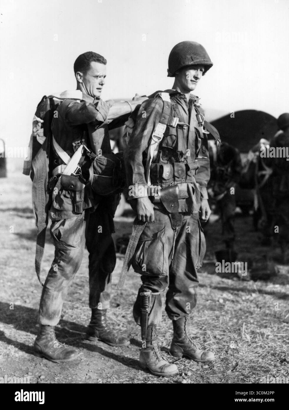 A U.S. paratrooper helping a fellow soldier to put on his parachute ...
