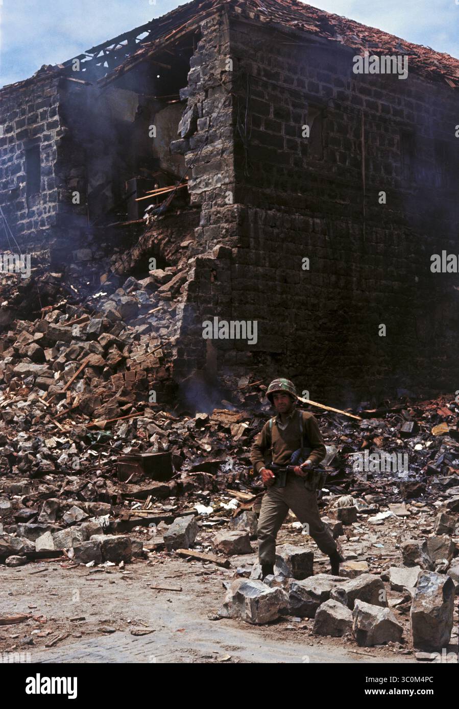 An Israeli soldier at the Syrian front, in front of a house destroyed ...