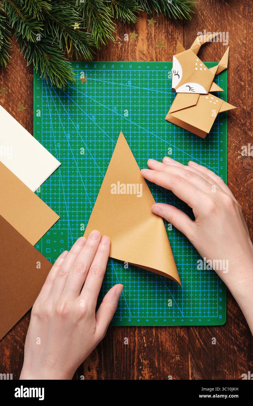 Hands folding brown paper for origami toys. In the background, a ...