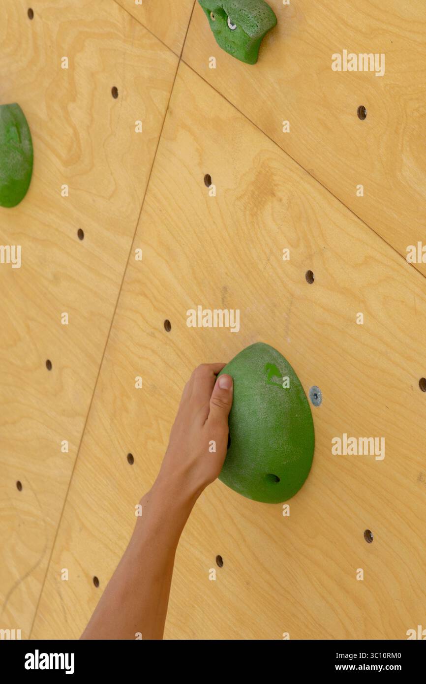 Child practicing climbing on an indoor wall, gripping a vibrant green ...
