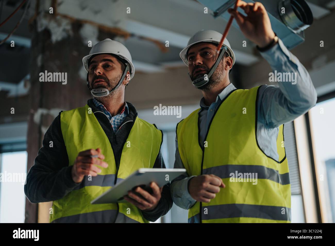 Two construction workers discussing a project plan on site, wearing ...