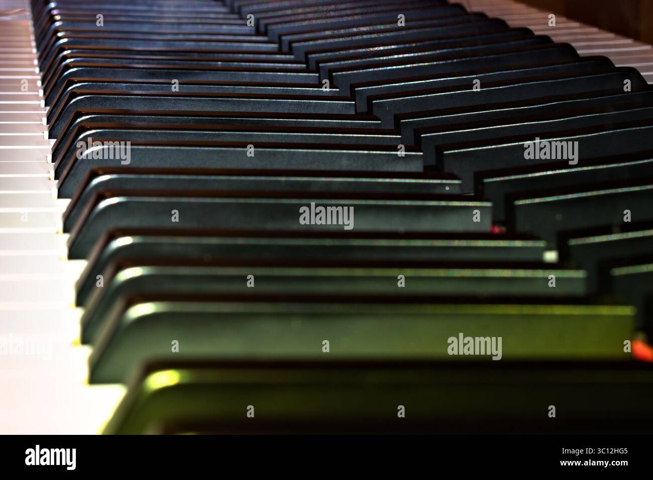 The black keys on a piano keyboard reflect off the black wood of the ...