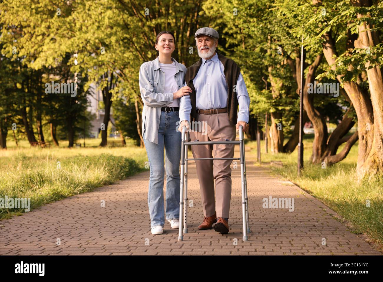 Smiling caregiver supporting elderly man who using walking frame ...