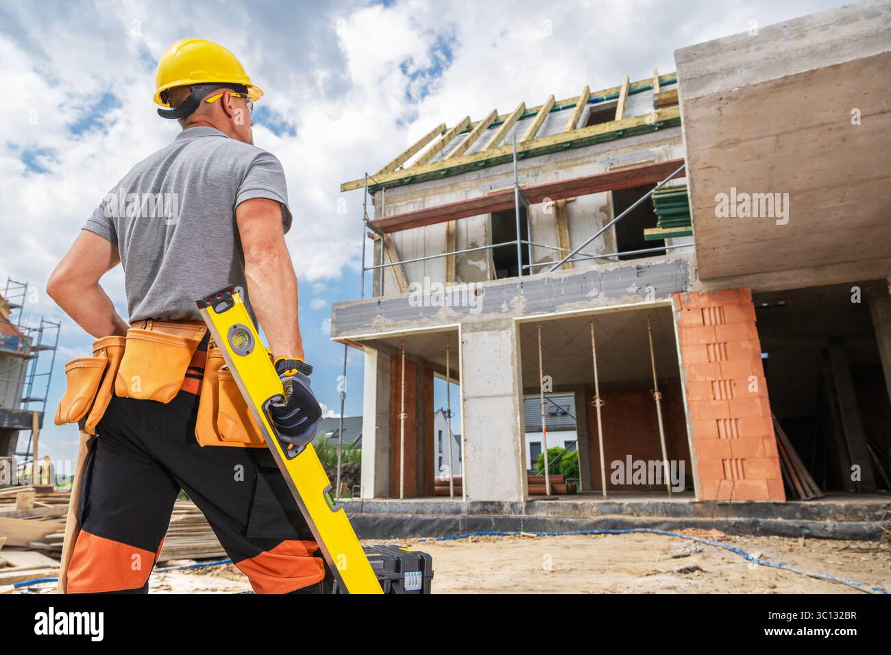 A construction worker stands observing a nearly finished building while ...