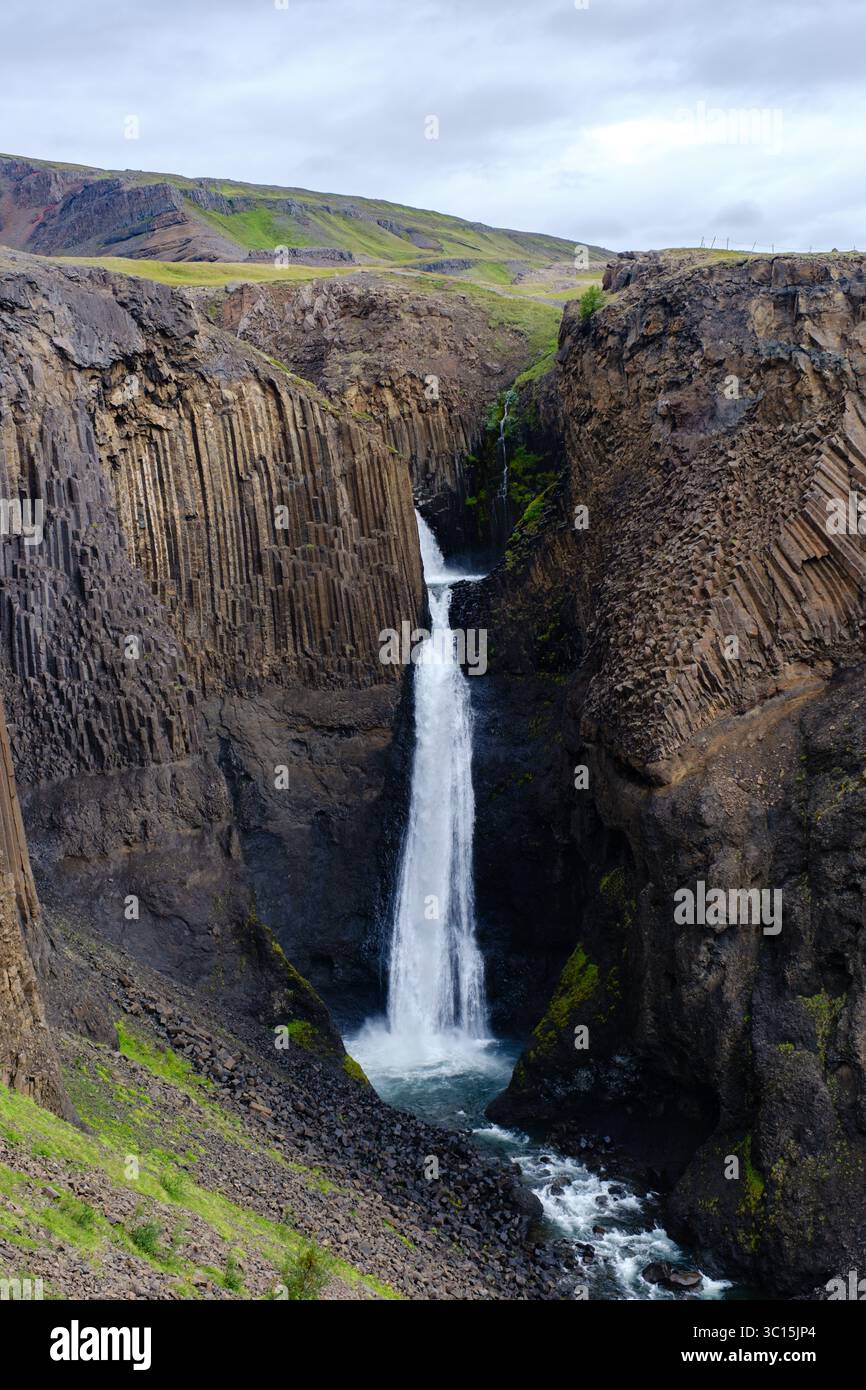Crystal clear water flows gracefully down a dramatic Hengifoss waterfall surrounded by towering ...