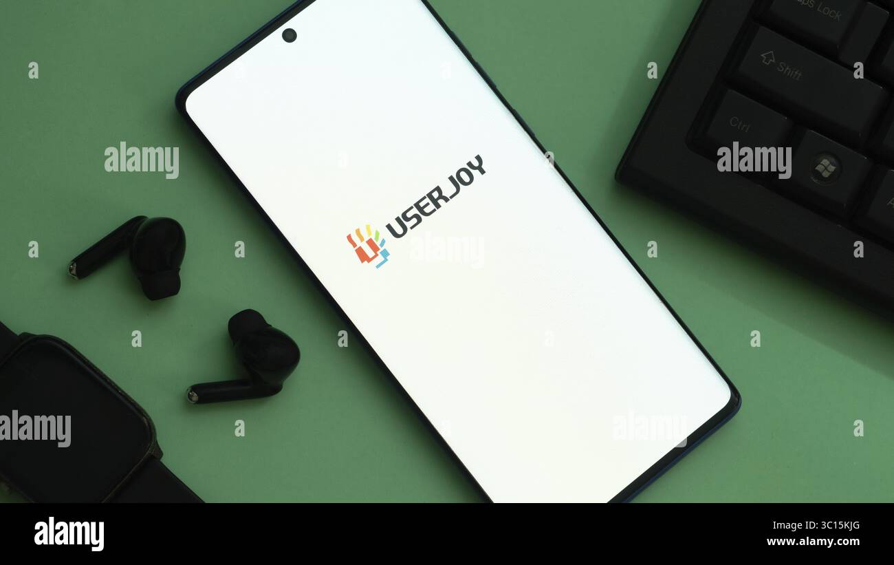 Smartphone displaying USERJOY logo on a white screen with earbuds and keyboard nearby Stock ...