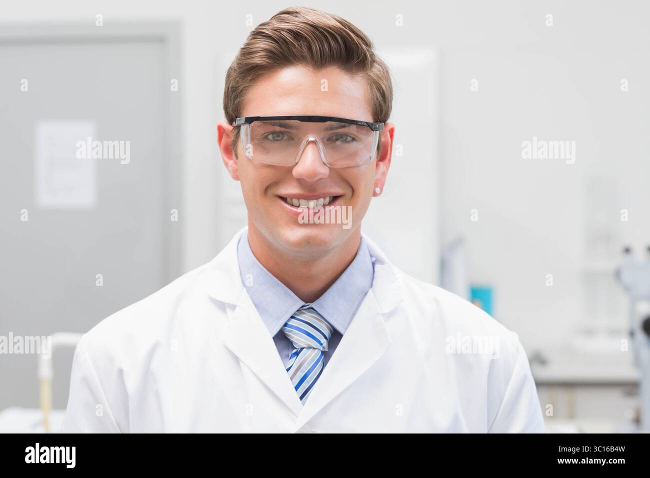 Male laboratory researcher standing at lab bench wearing white lab coat ...