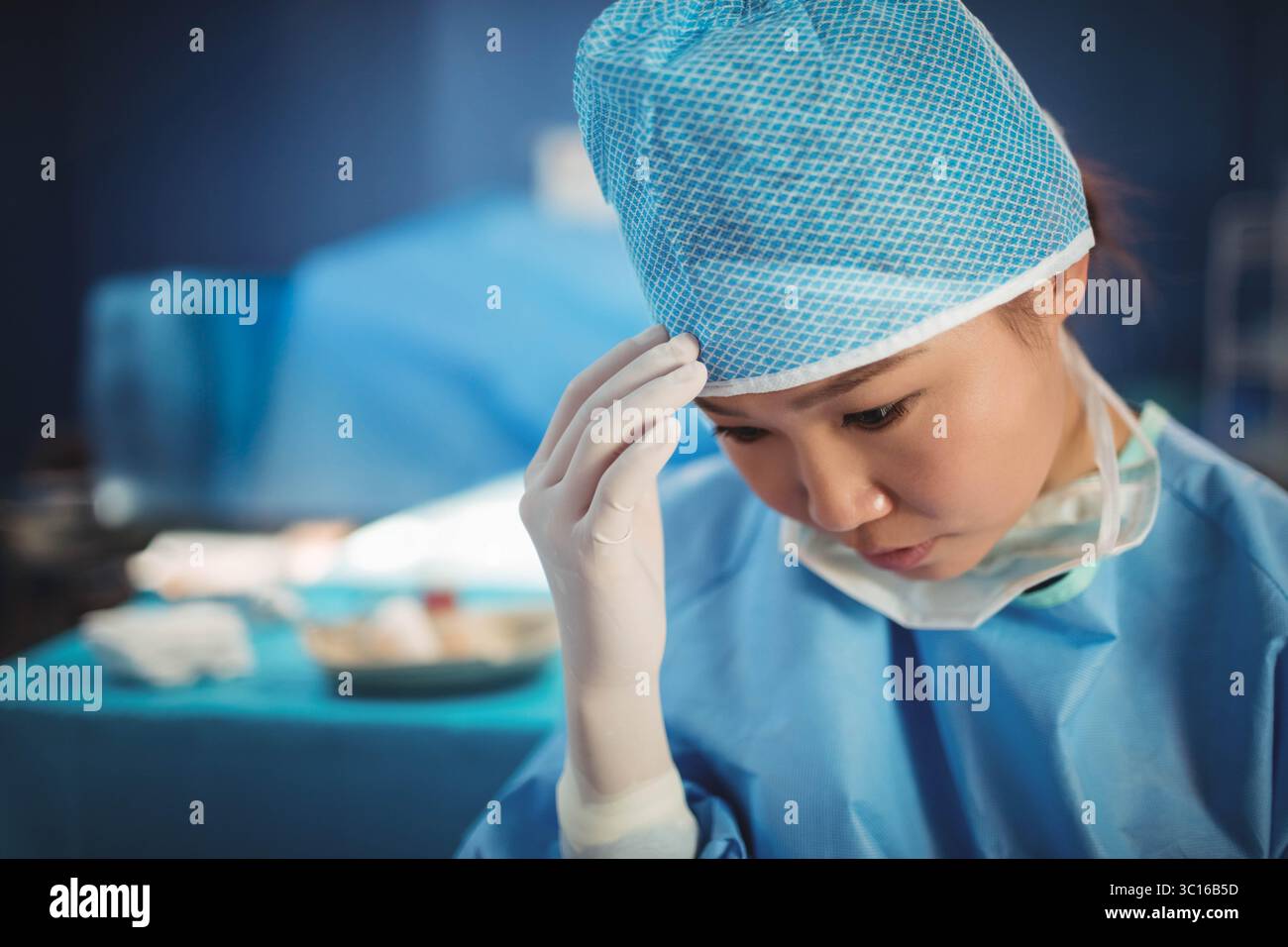surgeon wearing blue scrub cap pausing in operating room while touching ...