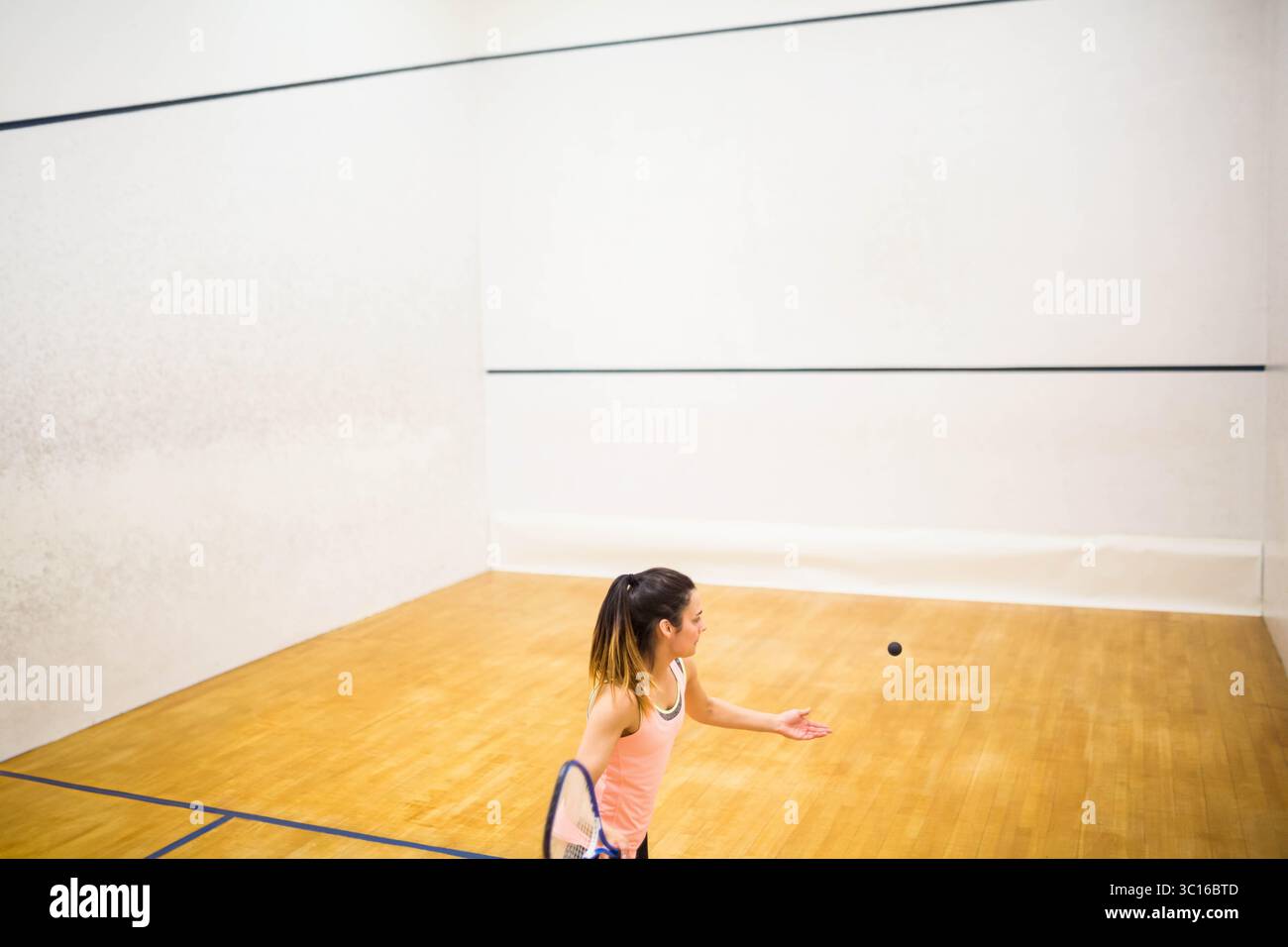 Female squash player is swinging racket to hit black squash ball on ...