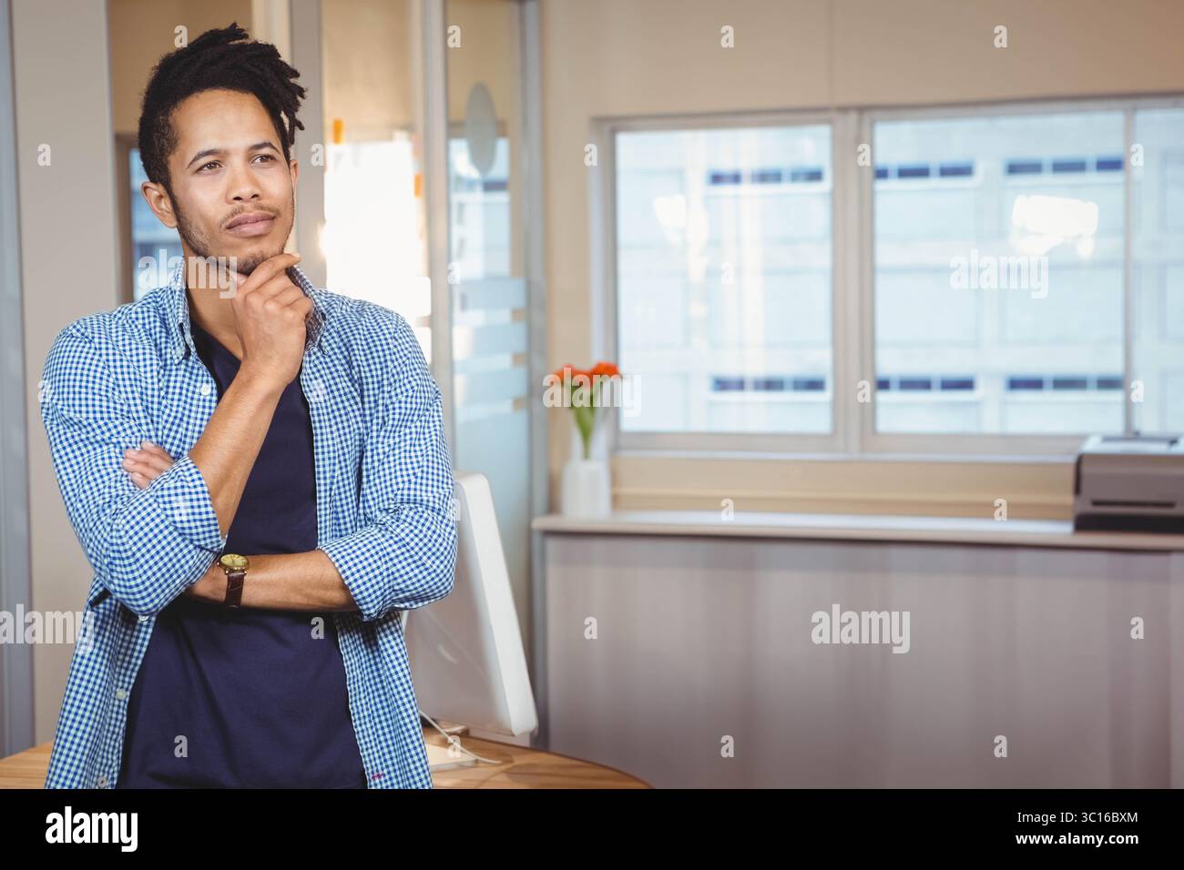 African American man gazing out at desk in office with monitor and ...