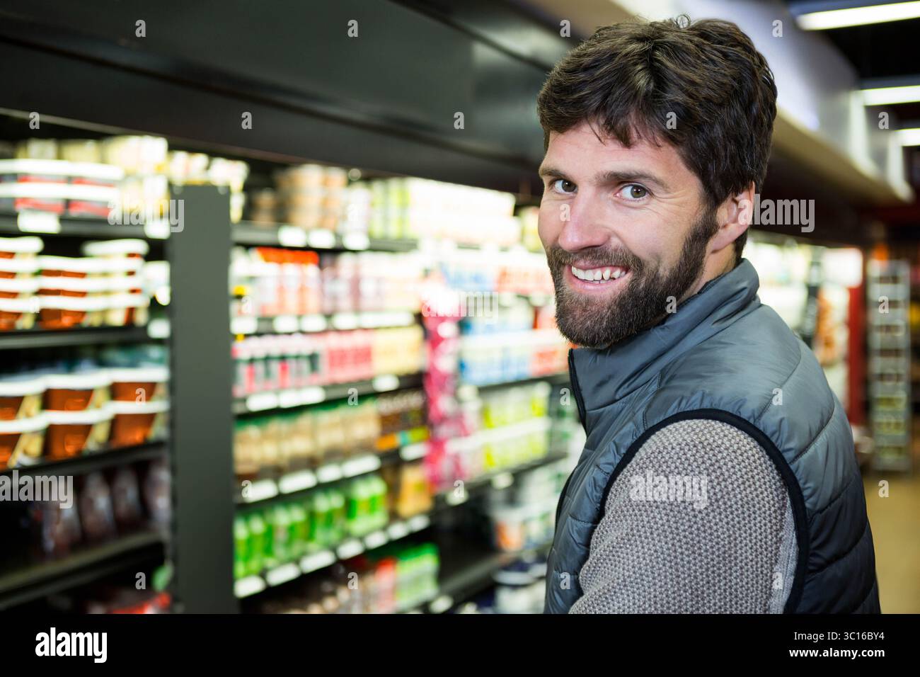 Male shopper standing in supermarket aisle wearing quilted vest and ...