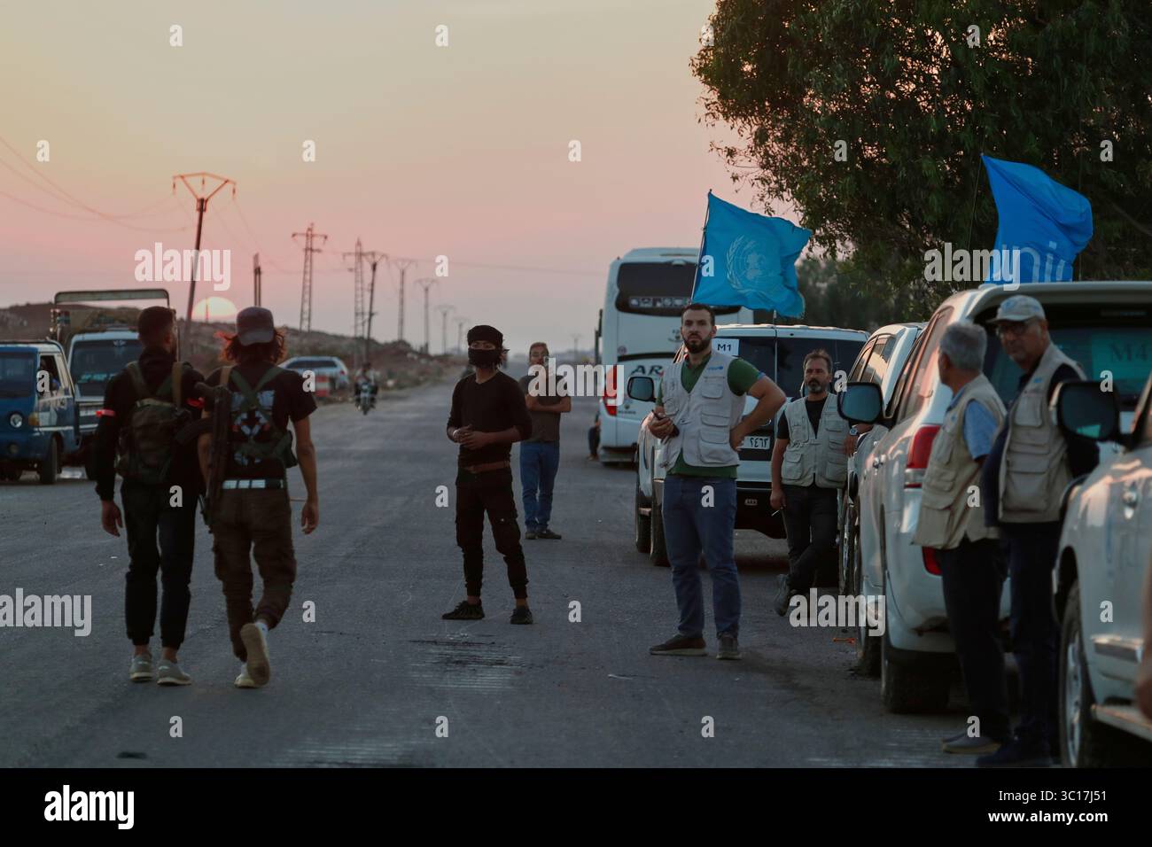 The sun sets as a convoy of ambulances and buses waits at a checkpoint ...