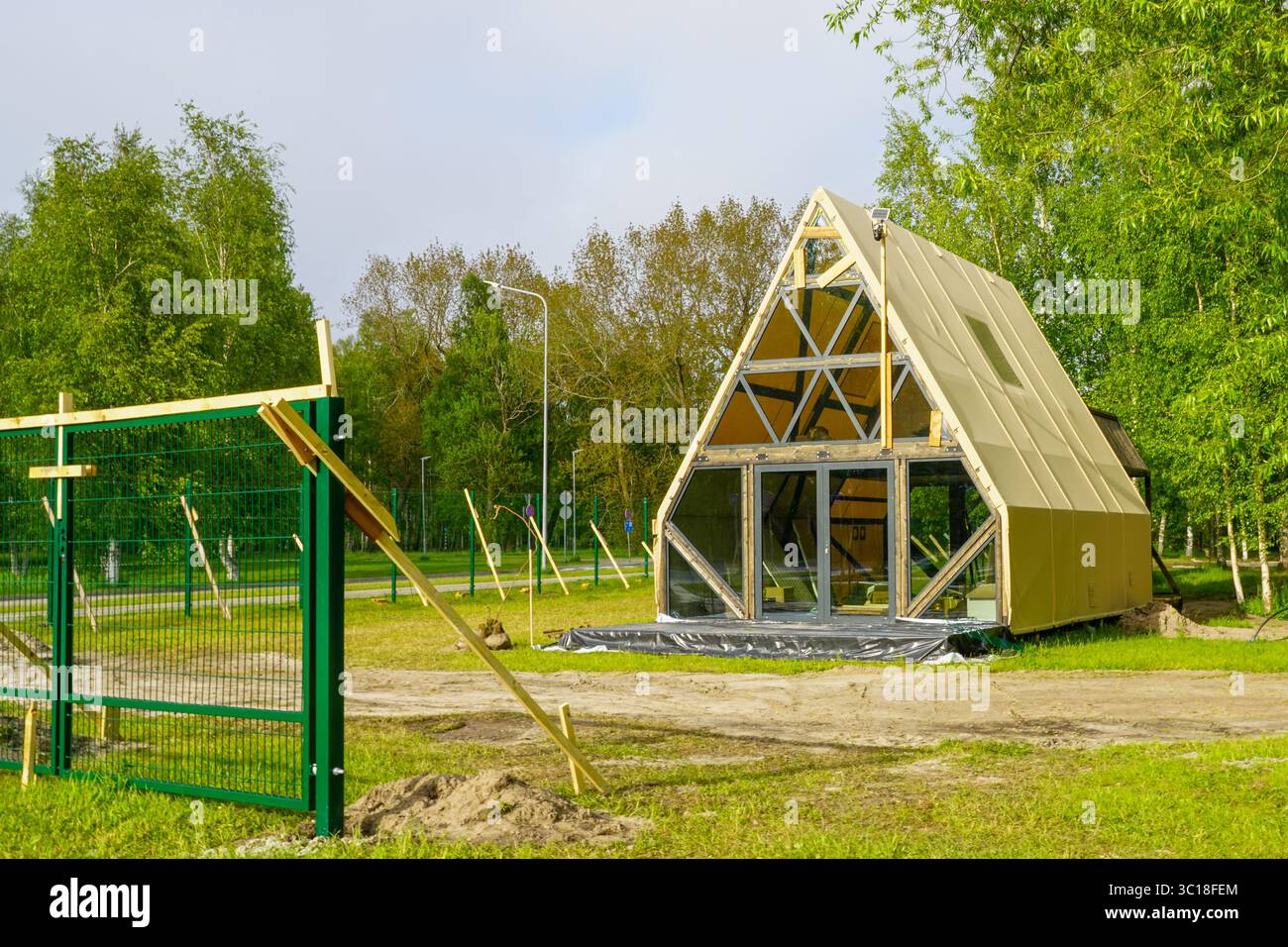 An A-frame cabin with glass walls is under construction, surrounded by ...