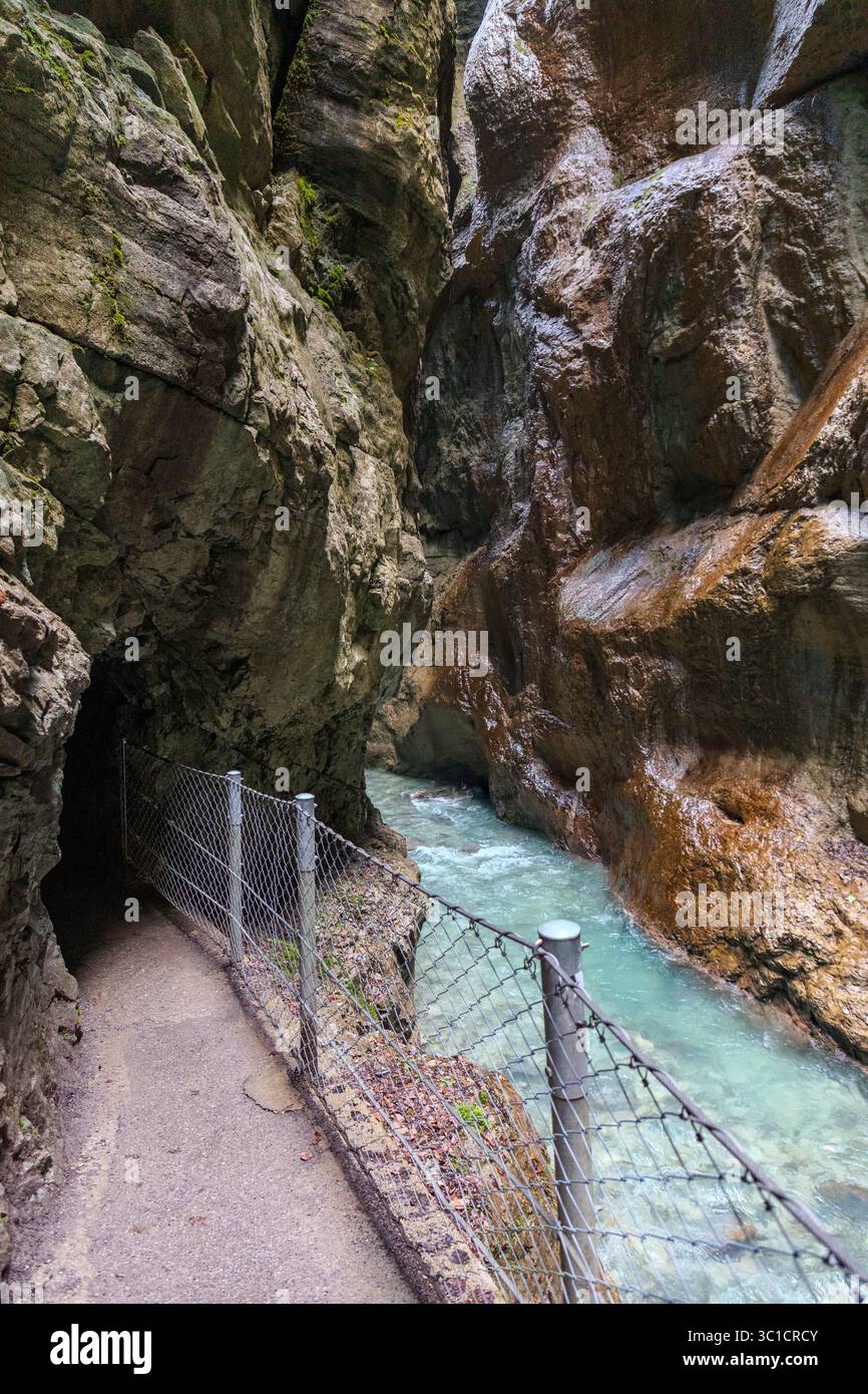 Narrow walkway carved into the cliffside along a turquoise stream ...