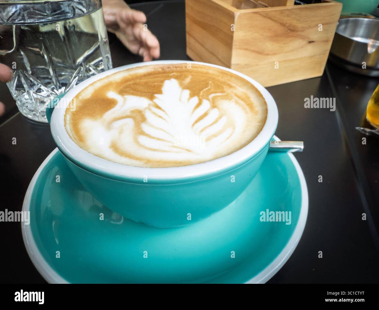 Turquoise cup filled with creamy cappuccino topped by leaf‑shaped latte ...