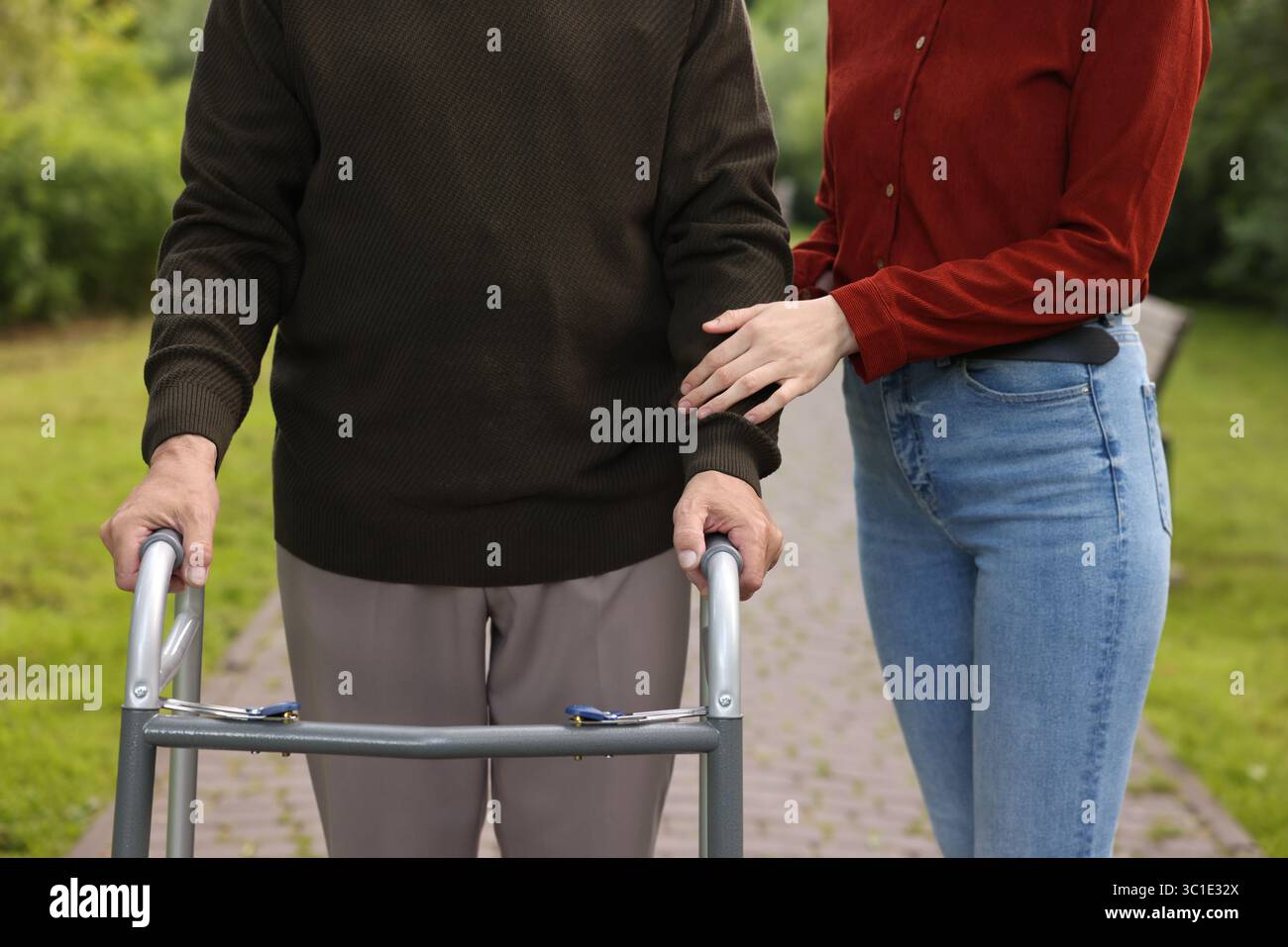 Caregiver supporting elderly man who using walking frame outdoors ...