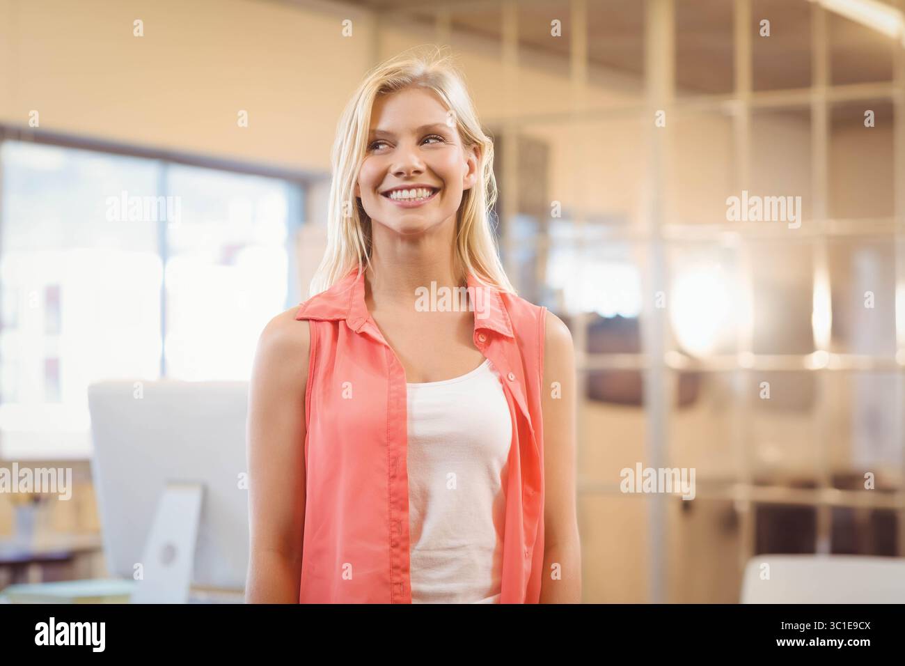 Female employee standing and smiling at open-plan workspace with ...