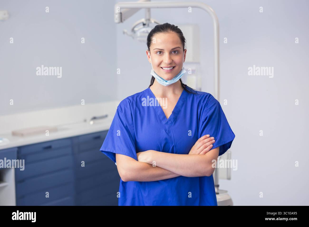 Female dentist standing in dental clinic wearing blue scrubs with mask ...