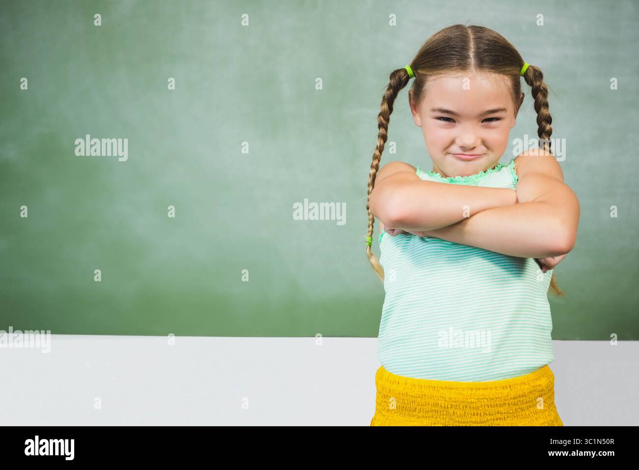 Female child standing with crossed arms in classroom at green ...