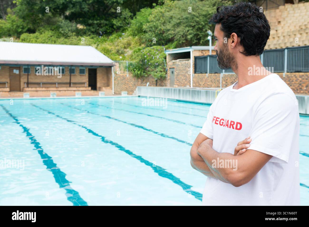 Lifeguard standing watch at edge of swimming pool, with lane markings ...