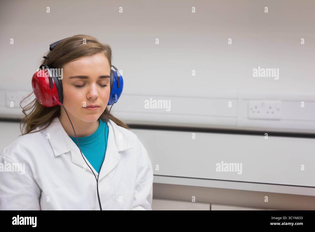 Woman wearing white lab coat, red blue earmuffs sitting with eyes ...