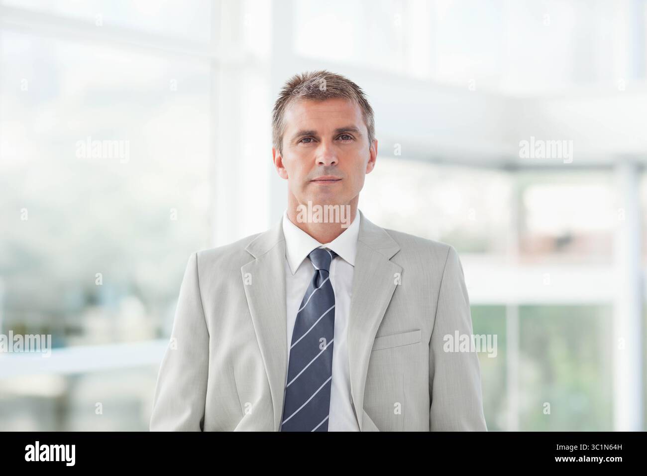 Middle-aged man standing wearing gray suit and striped tie in bright ...