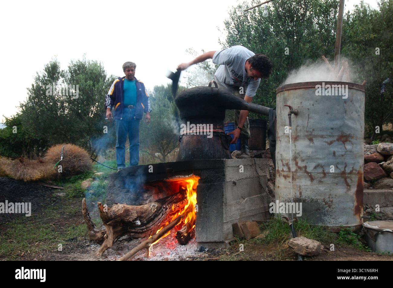 Two men operating a traditional outdoor raki distillery in Crete ...