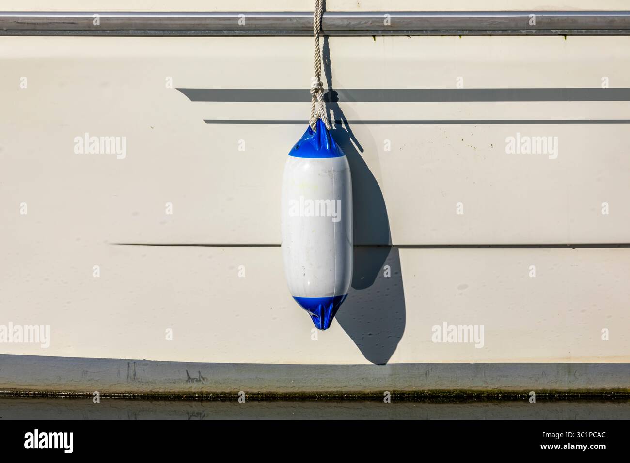 Close-up of a white and blue boat fender hanging from a rope against a ...